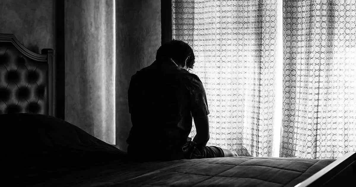 muž zažívá rozvod se pokusil, sedí na posteli a smutně se dívá z okna