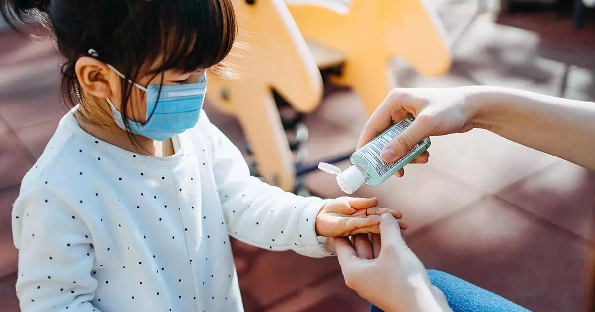 Einem Kleinkind, das eine Maske trägt, wird Händedesinfektionsmittel auf die Hand gespritzt